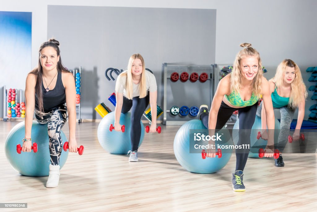 Four Women On Gymnastic Balls With Dumbbells Perform Exercises In The