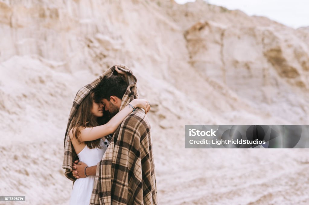 Beautiful Couple Embracing And Kissing Under Blanket In Sand Canyon