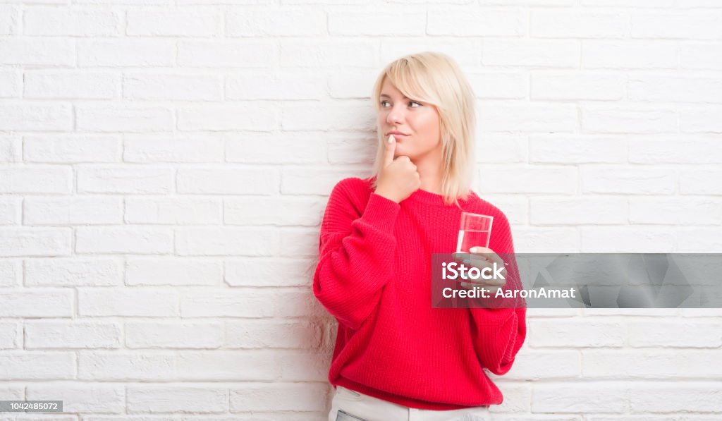 Adult Caucasian Woman Over White Brick Wall Drinking A Glass Of Water