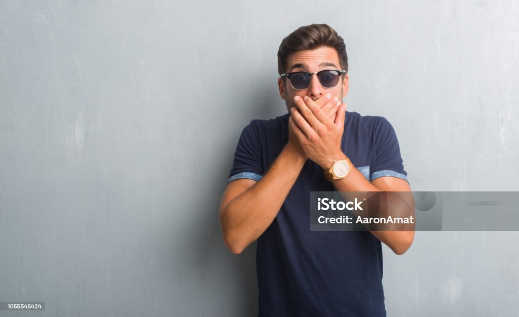 Handsome Young Man Over Grey Grunge Wall Wearing Sunglasses Shocked