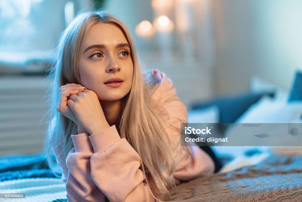 Young Cute Woman Lying Down On A Bed With Pillows Looking At Camera
