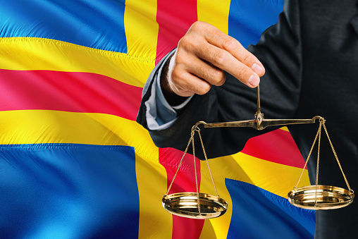 Judge Is Holding Golden Scales Of Justice With Aland Islands Waving