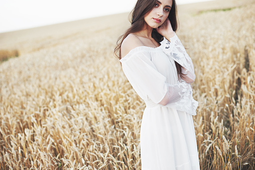 Young Sensitive Girl In White Dress Posing In A Field Of Golden Wheat
