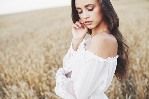 Young Sensitive Girl In White Dress Posing In A Field Of Golden Wheat