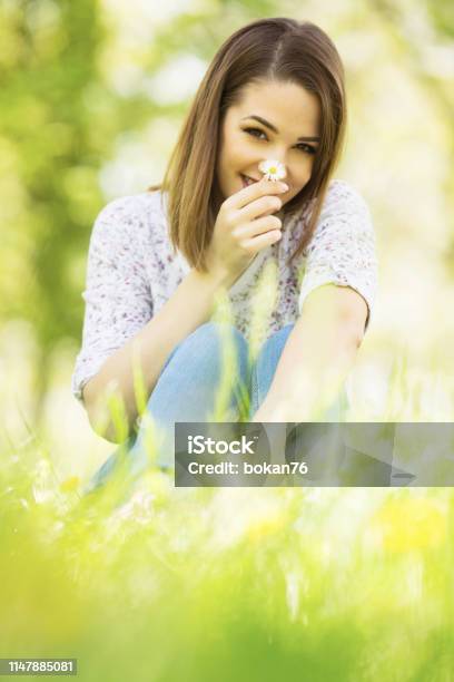 Wanita Muda Yang Cantik Dan Ceria Duduk Di Rumput Dan Memegang Bunga ... Wanita Muda Yang Cantik Dan Ceria Duduk Di Rumput Dan Memegang Bunga ...