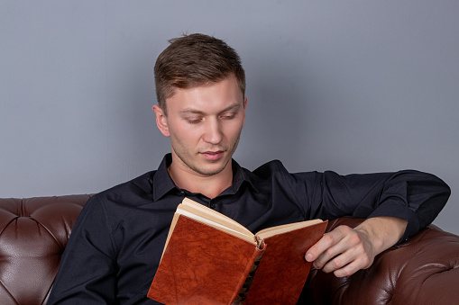 Genç Adam Bir Deri Kanepede Oturuyor Ve Kitap Okuyor Stok Fotoğraflar