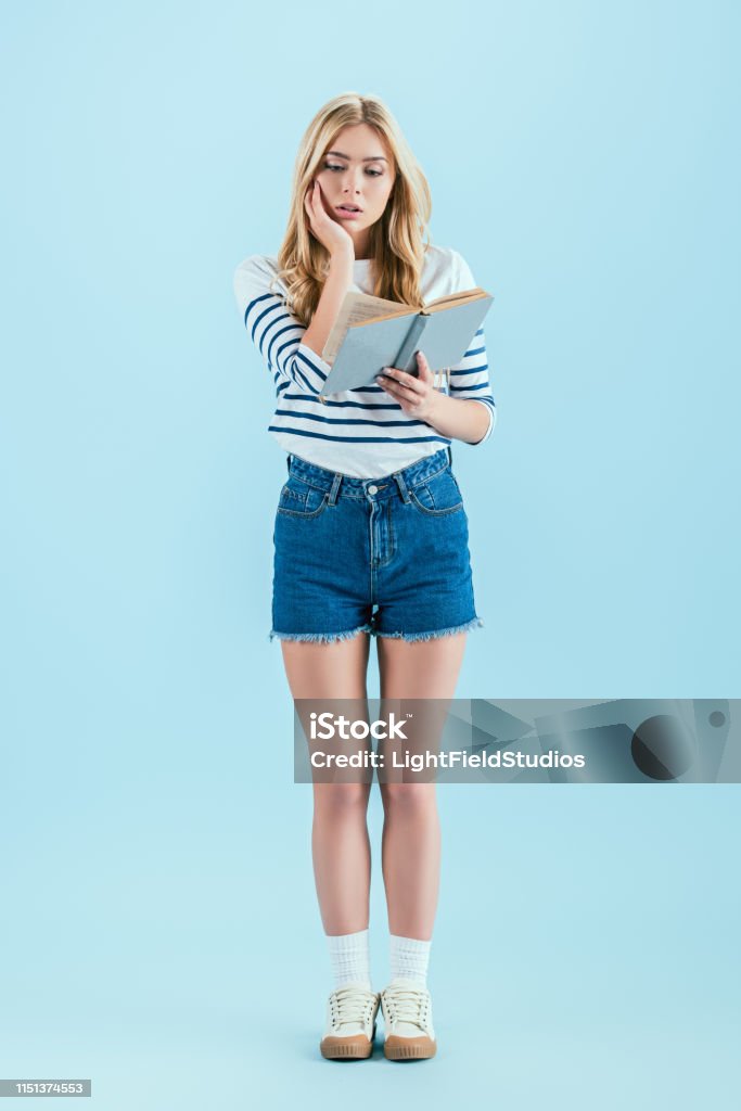 Full Length View Of Blonde Girl Reading Book On Blue Background Stock