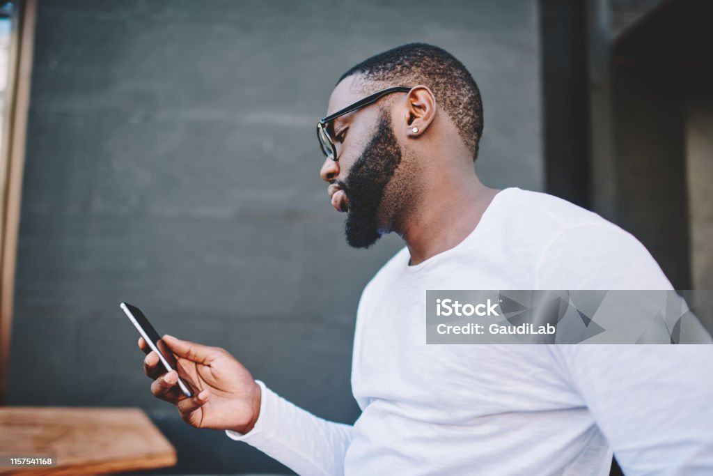 Side View Of Handsome African American Guy Reading Message On Phone