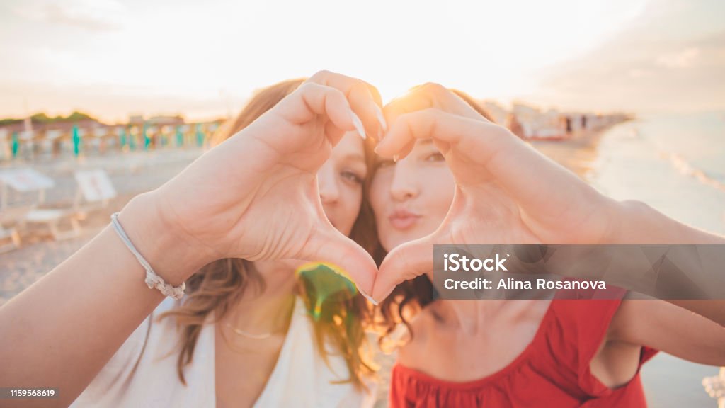 Beautiful Girlfriends On The Beach Making Heart Shape With Hands