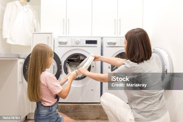 Mother And Daughter Helper In Laundry Room Near Washing Machine And