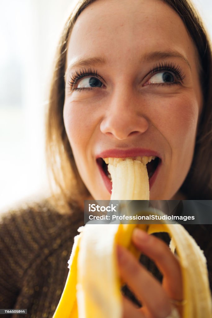 Wanita Muda Yang Bugar Mengupas Dan Makan Pisang Matang Di Dapur Foto
