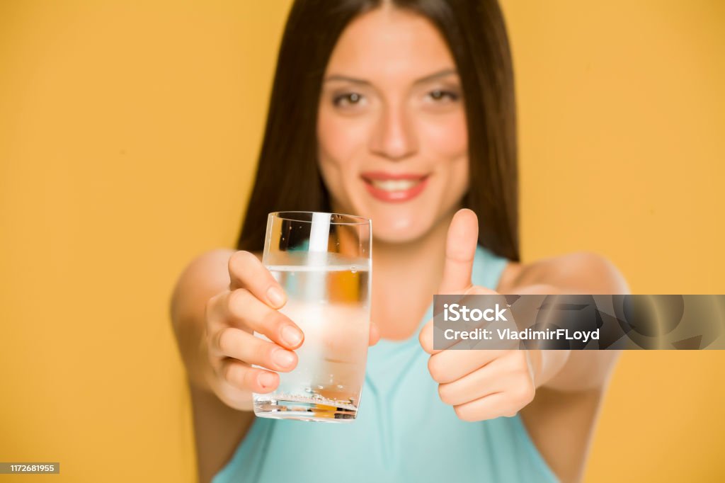 Young Smiling Woman Holding Glass Of Water And Showing Thumbs Up On