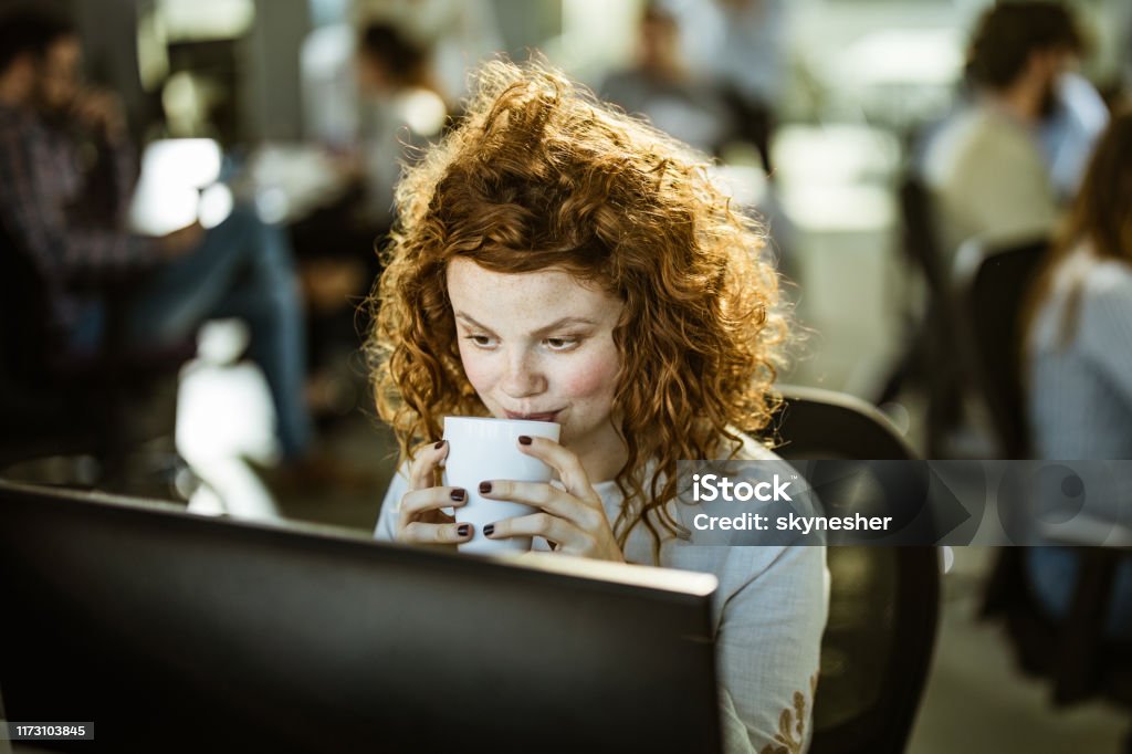 Smiling Redhead Programmer Drinking Coffee While Working On Desktop Pc ... Smiling Redhead Programmer Drinking Coffee While Working On Desktop Pc ...