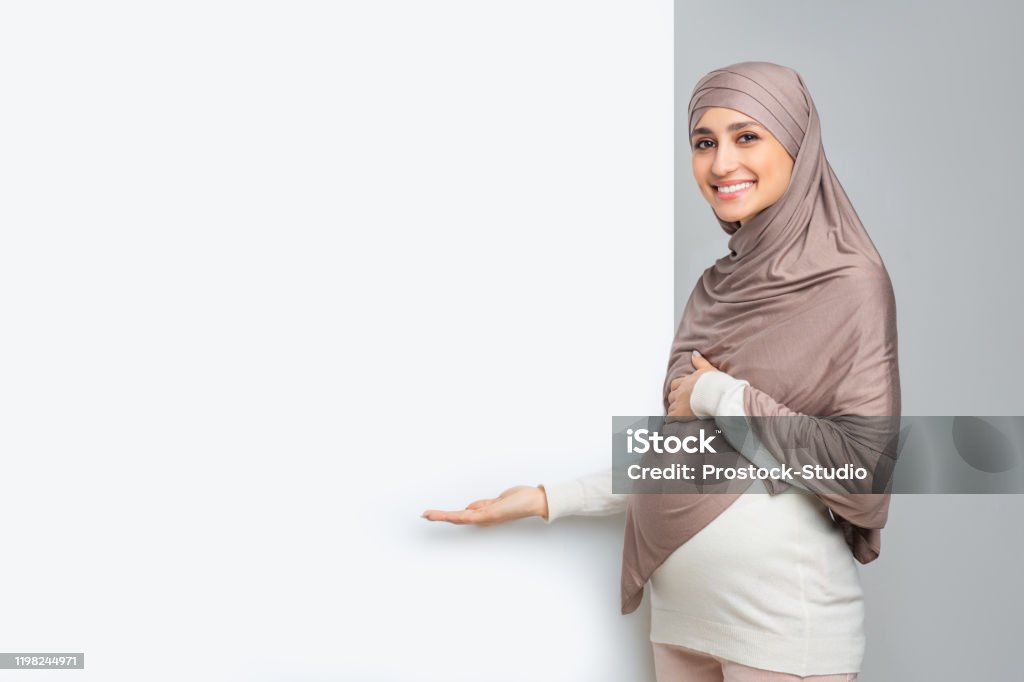 Pregnant Islamic Girl In Hijab Pointing At White Advertisement Board