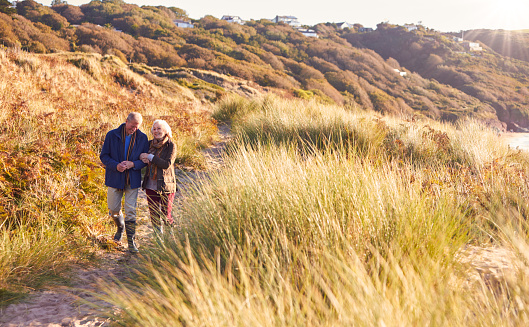 Loving Active Senior Couple Arm In Arm Walking Through Sand Dunes Stock