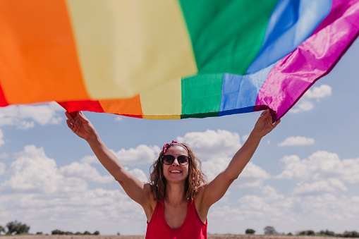 Woman Holding The Gay Rainbow Flag Over Blue And Cloudy Sky Outdoors