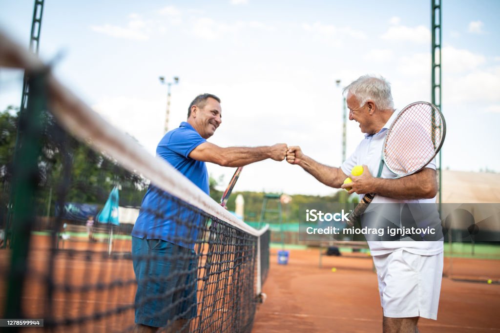 Two Senior Men Greeting Each Other With Fist Bump On Tennis Court Stock