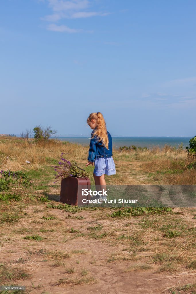 Little Blonde Girl In Denim Jacket Blue Dress With Vintage Suitcase And Flowers Bouquet Offroad