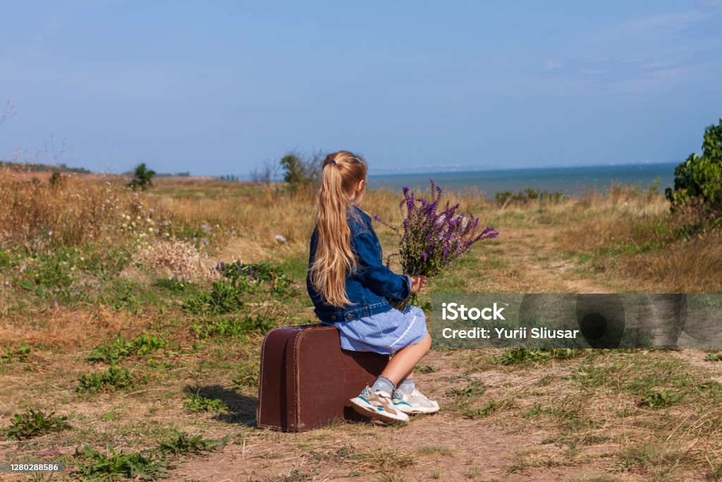 Little Blonde Girl In Denim Jacket Blue Dress With Vintage Suitcase And Flowers Bouquet Offroad