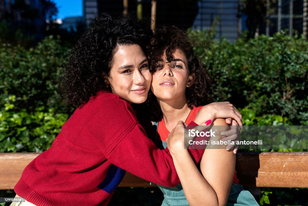 Smiling Lesbian Couple Embracing And Relaxing On A Park Bench Stock