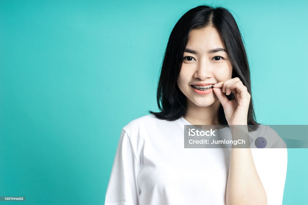 Asian Woman Wearing Dental Braces Pointing To Tooth Sample And Smiling