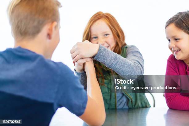 Three Siblings Arm Wrestling Together At Dining Table Photo Series