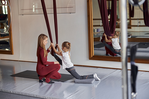 Young Gymnastics Teacher Is Helping A Girl To Do Exercises Indoors