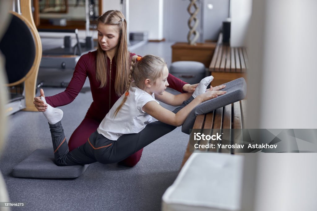 Young Gymnastics Teacher Is Helping A Girl To Do Exercises Indoors