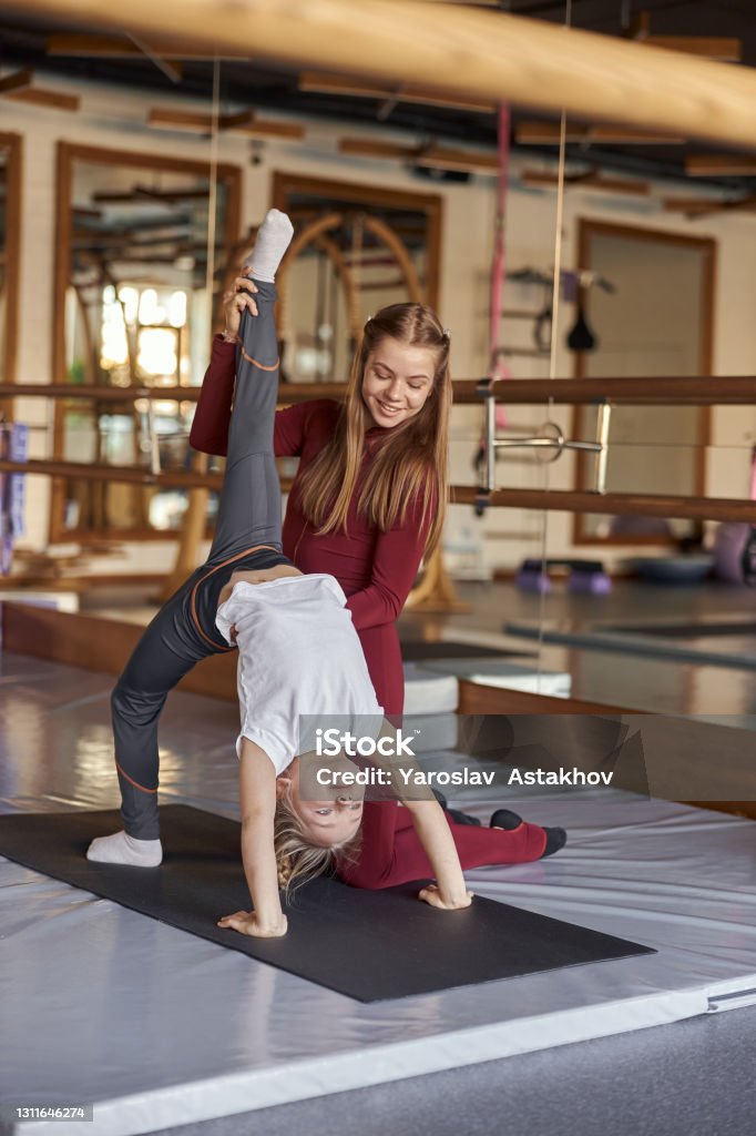 Young Gymnastics Teacher Is Helping A Girl To Do Exercises Indoors