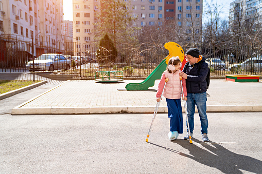 Dad Helps Daughter Learn To Walk On Crutches Plaster On Your Feet Stock