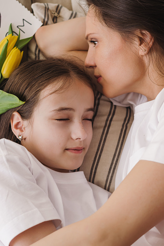 Happy Darkhaired Young Woman Hugs Her Daughter Lying At Home On The Bed