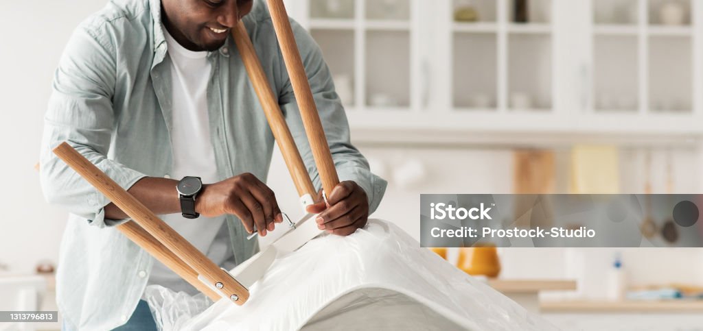 Black Handyman Screwing Detail To Chair In Kitchen Interior Panorama