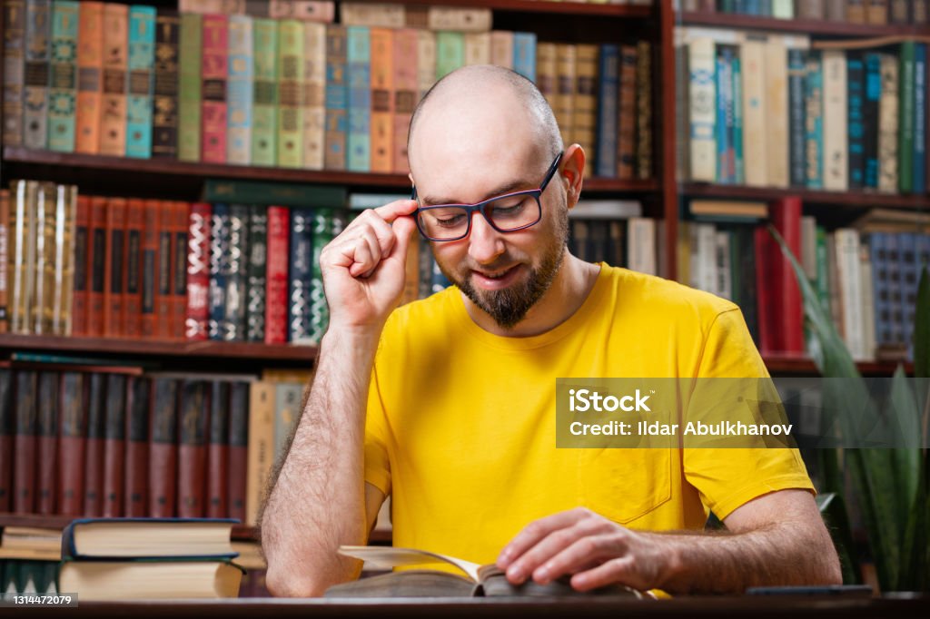 A Happy Bald Bearded Man With Glasses Is Reading A Book With His Hands