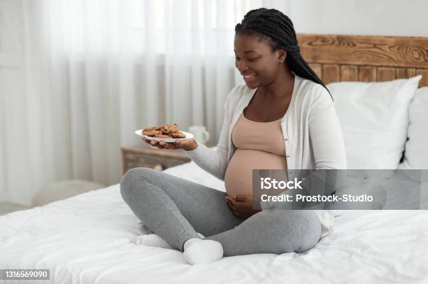 집에서 침대에 앉아있는 쿠키 접시를 가진 검은 임신 한 여성 임신에 대한 스톡 사진 및 기타 이미지 임신 먹고 싶어하는