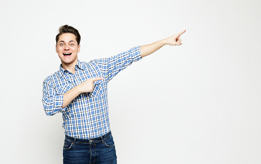 Happy And Surprised Handsome Man In Blue Shirt Turn Yout Attention At Banner Pointing Fingers