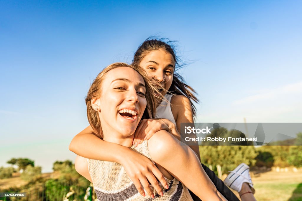 Two Girls Best Friends Having Fun Outdoor In A Green Nature Park Looking At Camera Laughing And
