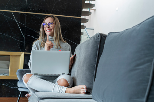 Wanita Yang Duduk Di Sofa Di Ruang Tamunya Saat Bekerja Dari Laptopnya ... Wanita Yang Duduk Di Sofa Di Ruang Tamunya Saat Bekerja Dari Laptopnya ...
