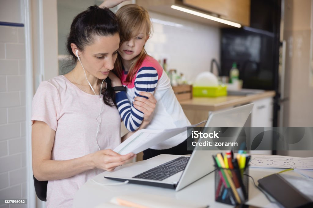 Single Mother Working On Laptop From Home Distracted By Her Daughter