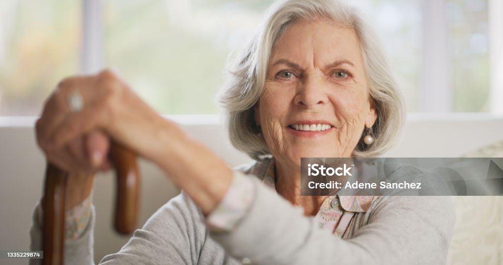 Shot Of An Elderly Woman Sitting On Her Sofa Holding Her Walking Stick