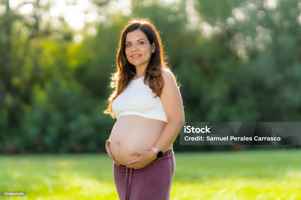 Pregnant Woman Touching Her Belly While Looking At The Camera Outdoors