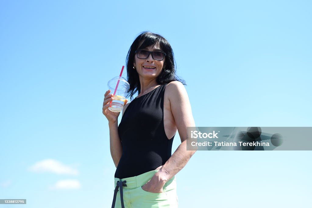 45 Years Old Russian Woman Drinking Lemonad And Standing Against Blue