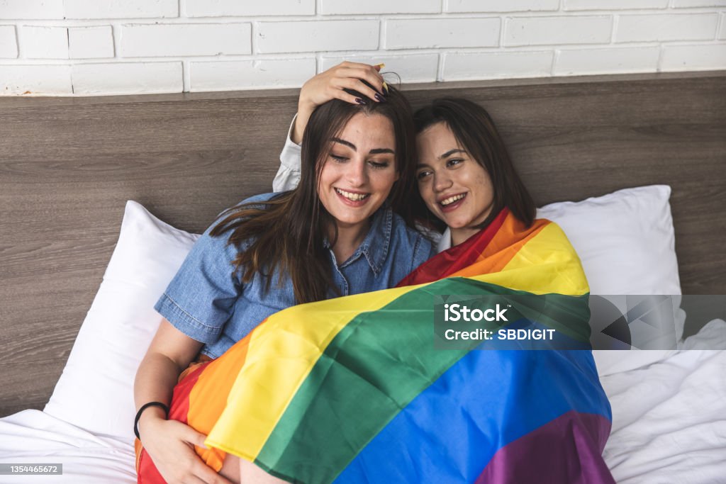 Lgbt Couple Cuddling And Enjoying In Hotel Room With Rainbow Flag Stock
