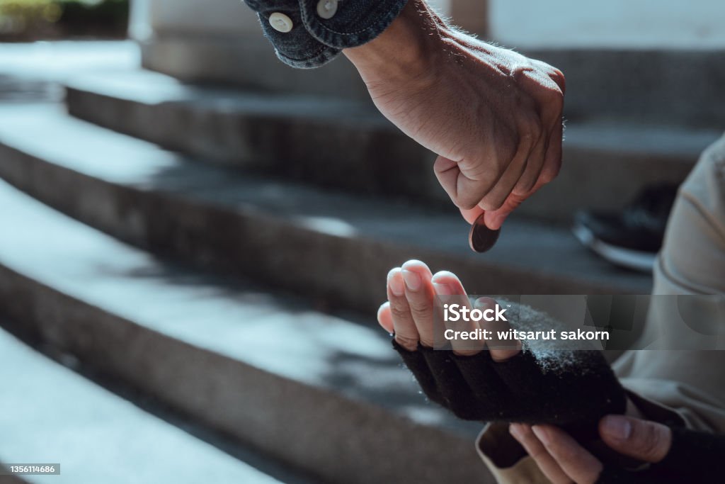 Young Man Giving Money To Homeless Beggar Man Sitting In Citygiving