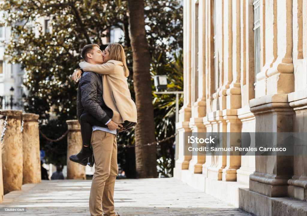 Young Man Kisses His Girlfriend While Holding Her In His Arms Stock