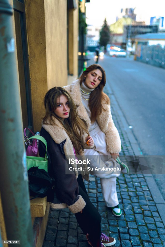 Portrait Of Young Stylish Young Women Leaning Against Wall On Street