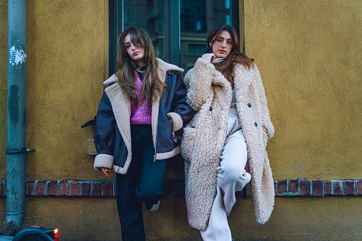 Portrait Of Young Stylish Young Women Leaning Against Wall On Street