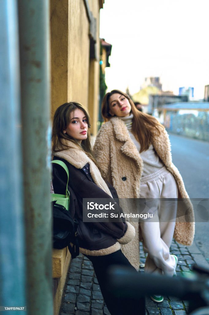 Portrait Of Young Stylish Young Women Leaning Against Wall On Street