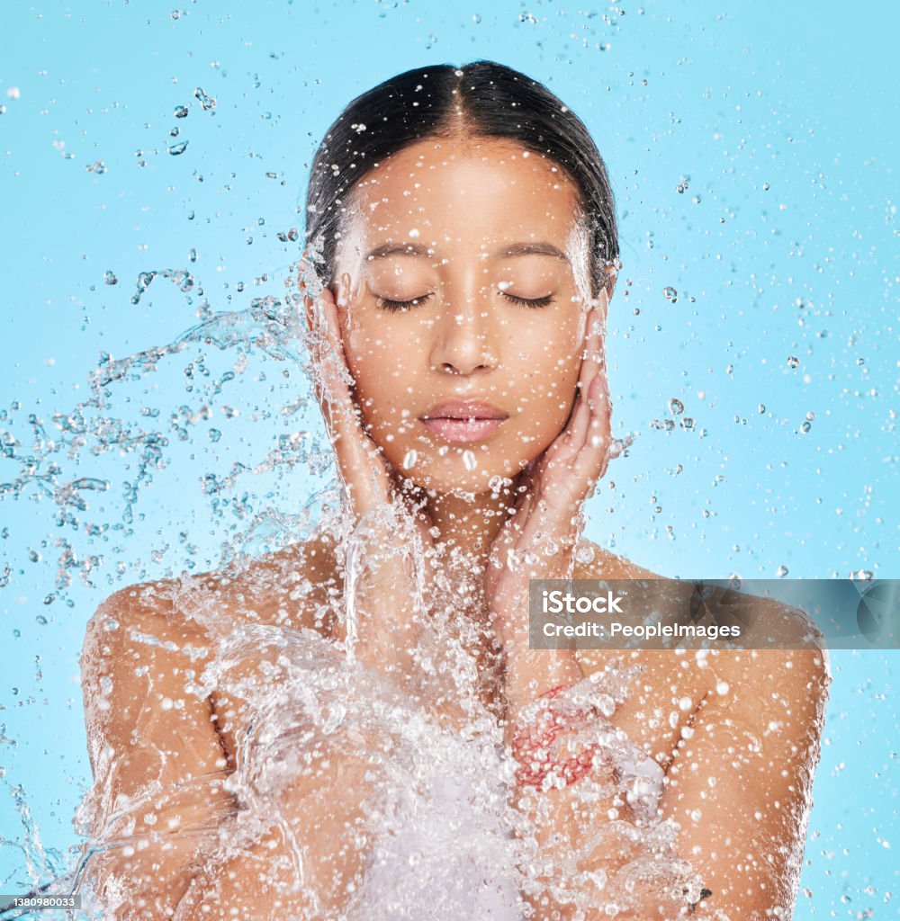 Shot Of A Beautiful Young Woman Being Splashed With Water Against A