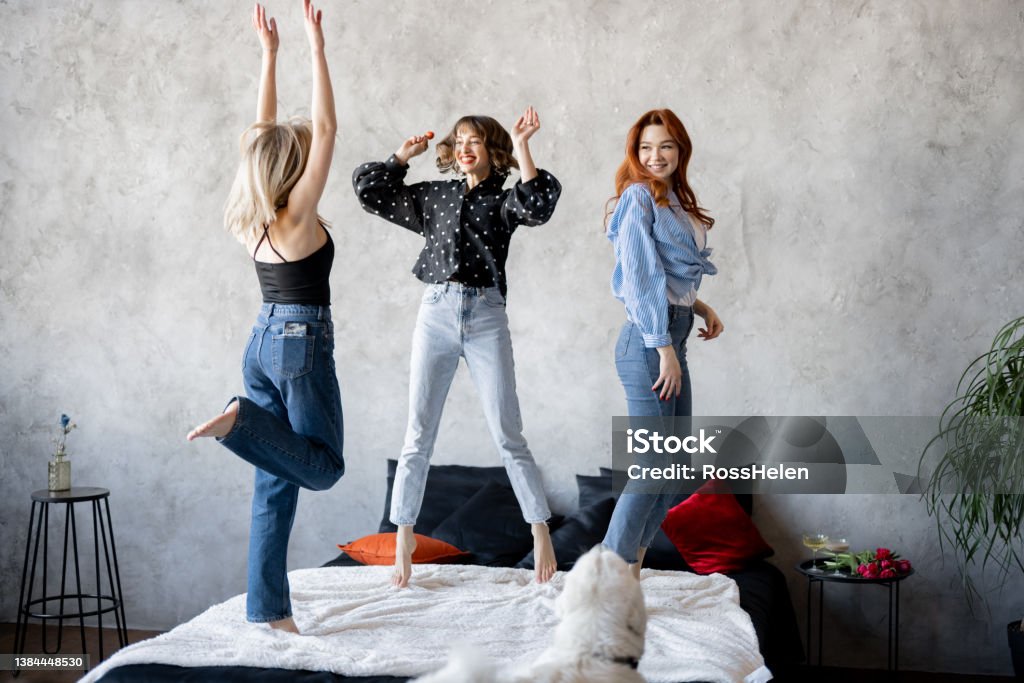 Adult Girlfriends Having Fun Jumping Together On Bed At Home Stock