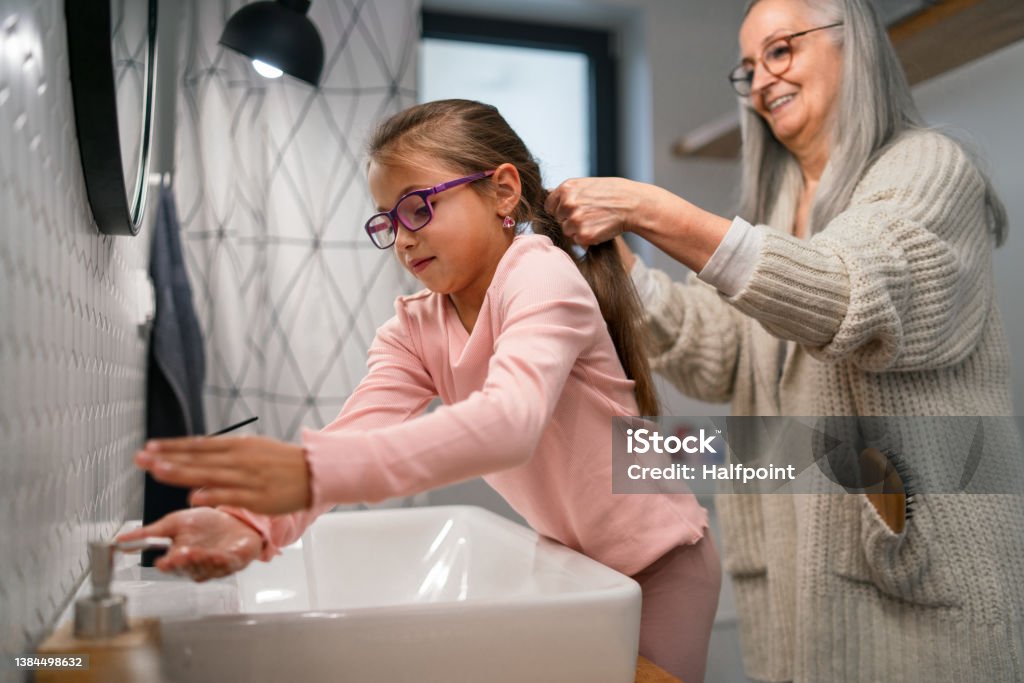Senior Grandmother And Granddaughter Standing Indoors In Bathroom Daily
